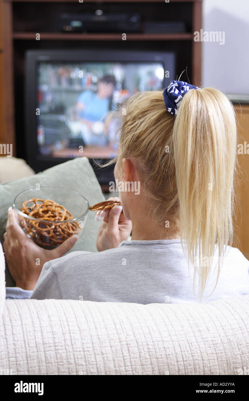 woman watching tv snacking, having some pretzel in the evening at home ...