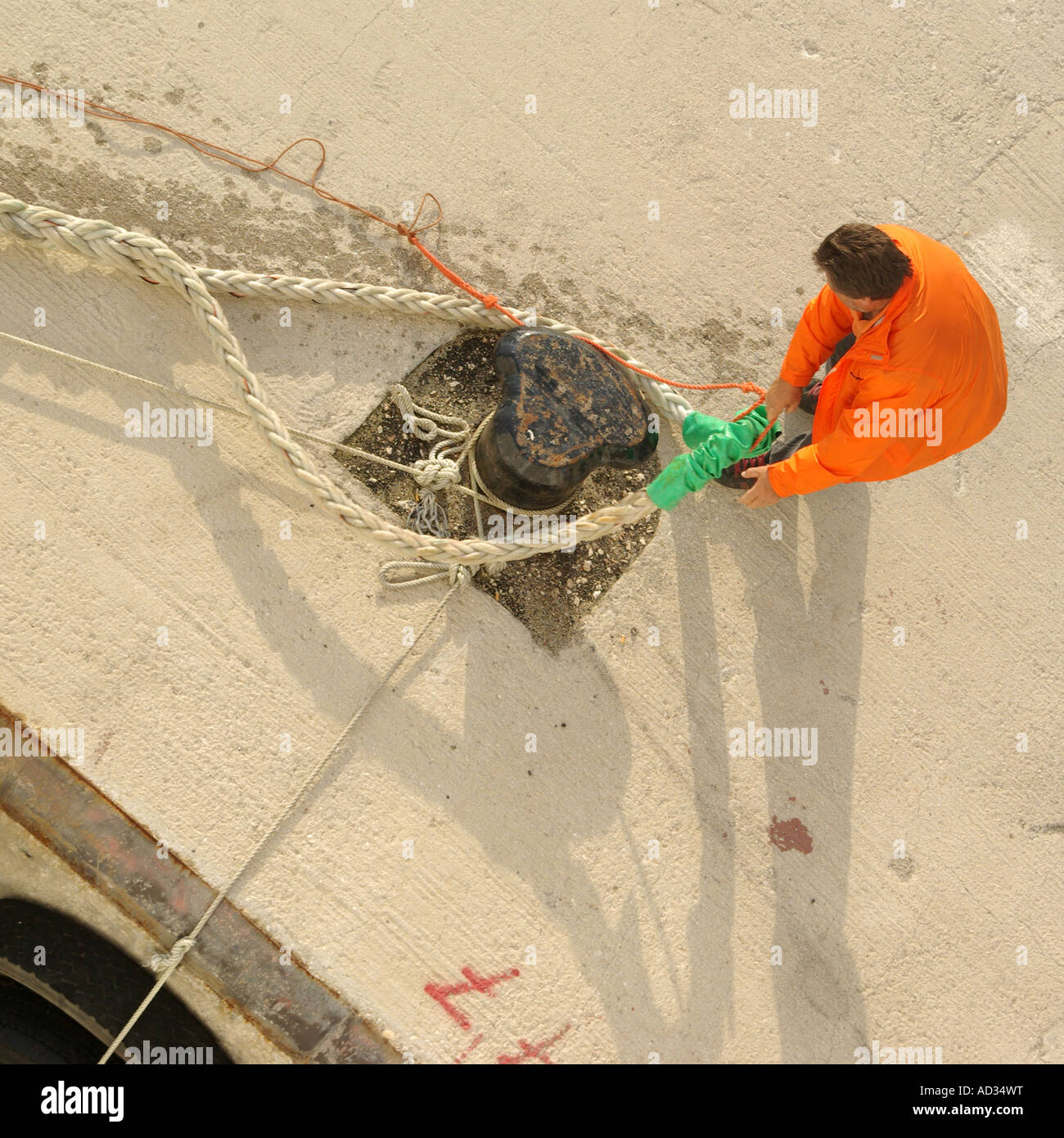 Dock worker on quayside manhandling heavy hawser onto capstan Stock ...