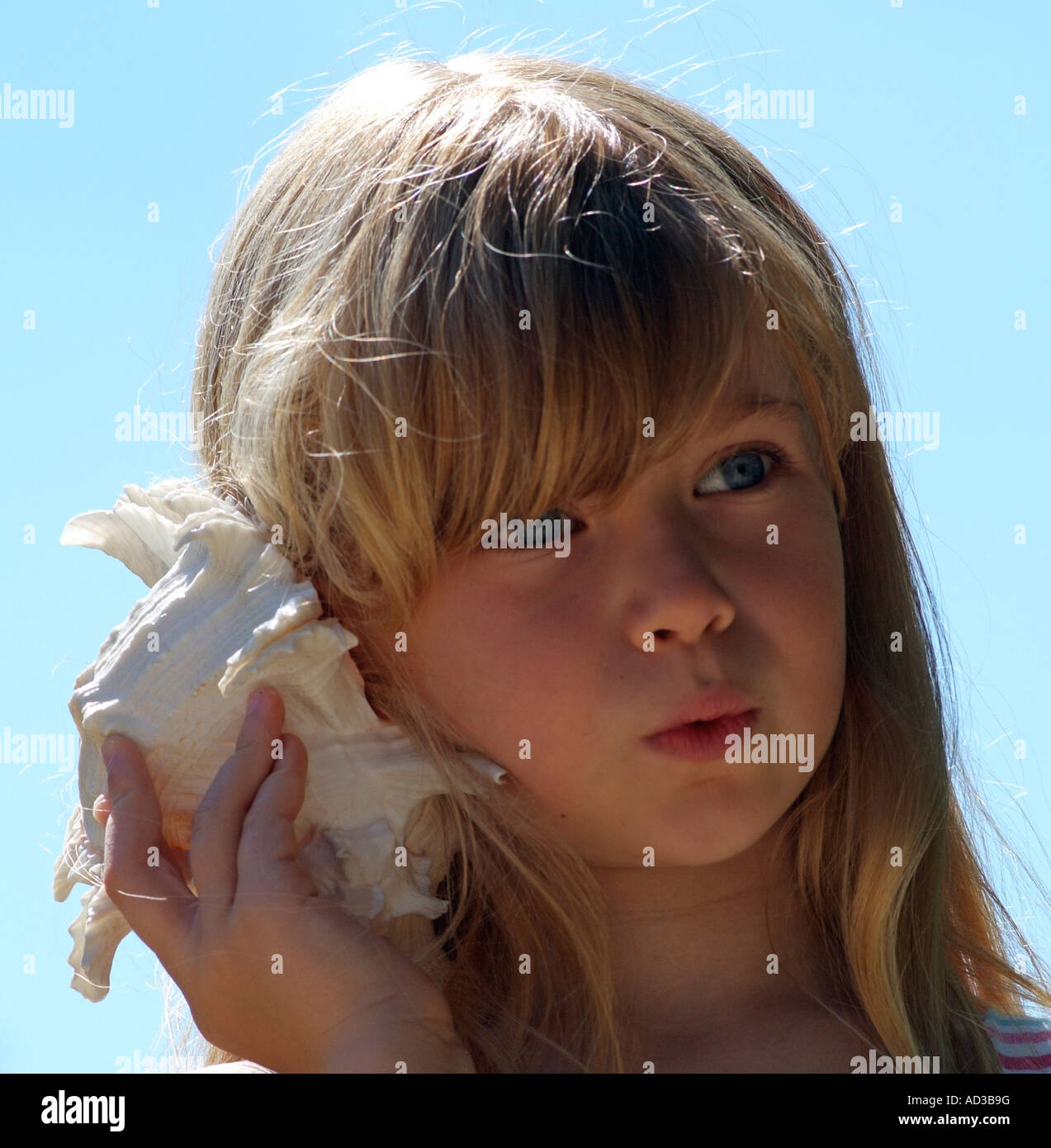 Little girl holding a seashell to her ear Listens to the sound of the ...