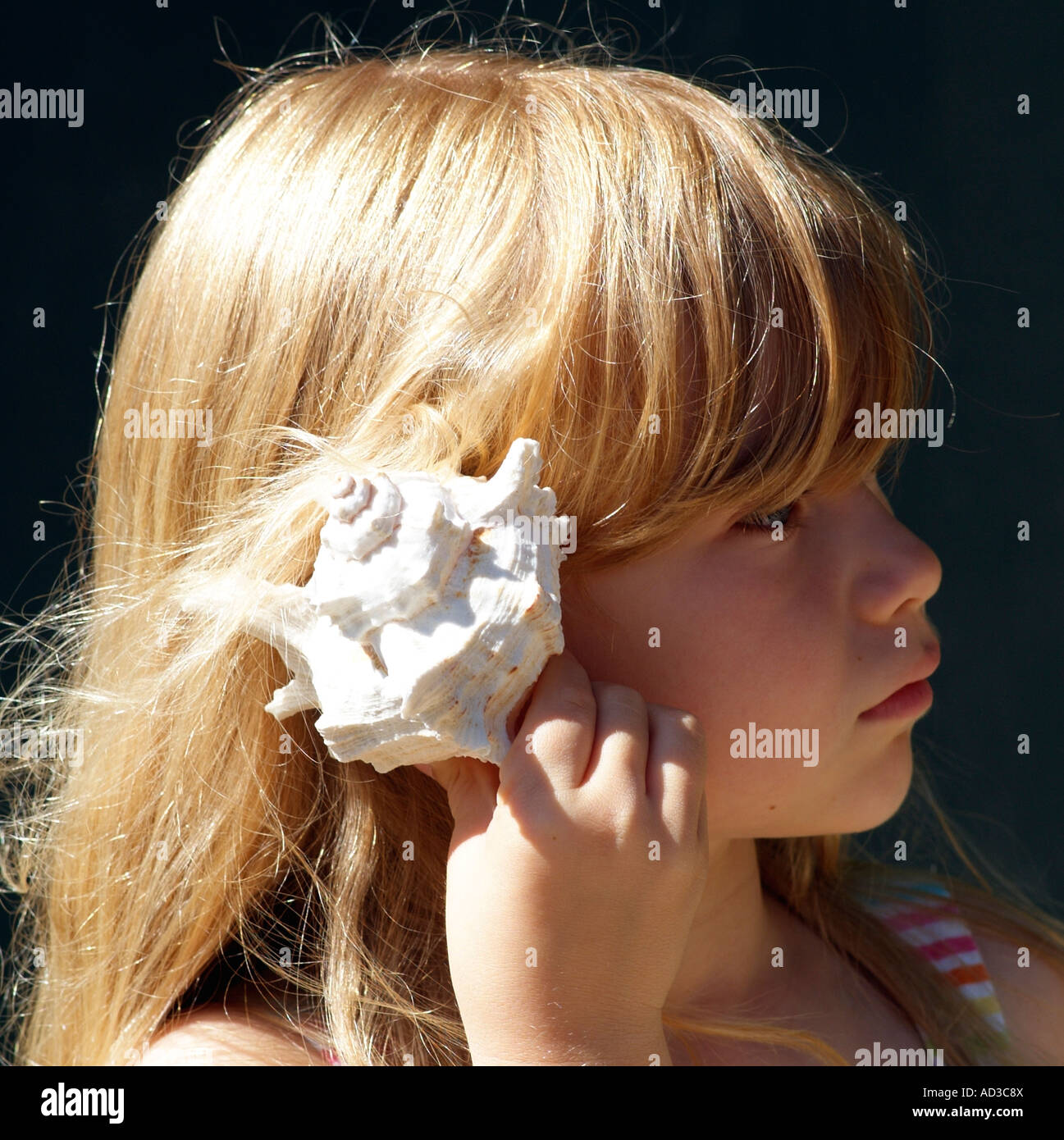 Little girl holding a seashell to her ear Listens to the sound of the ...