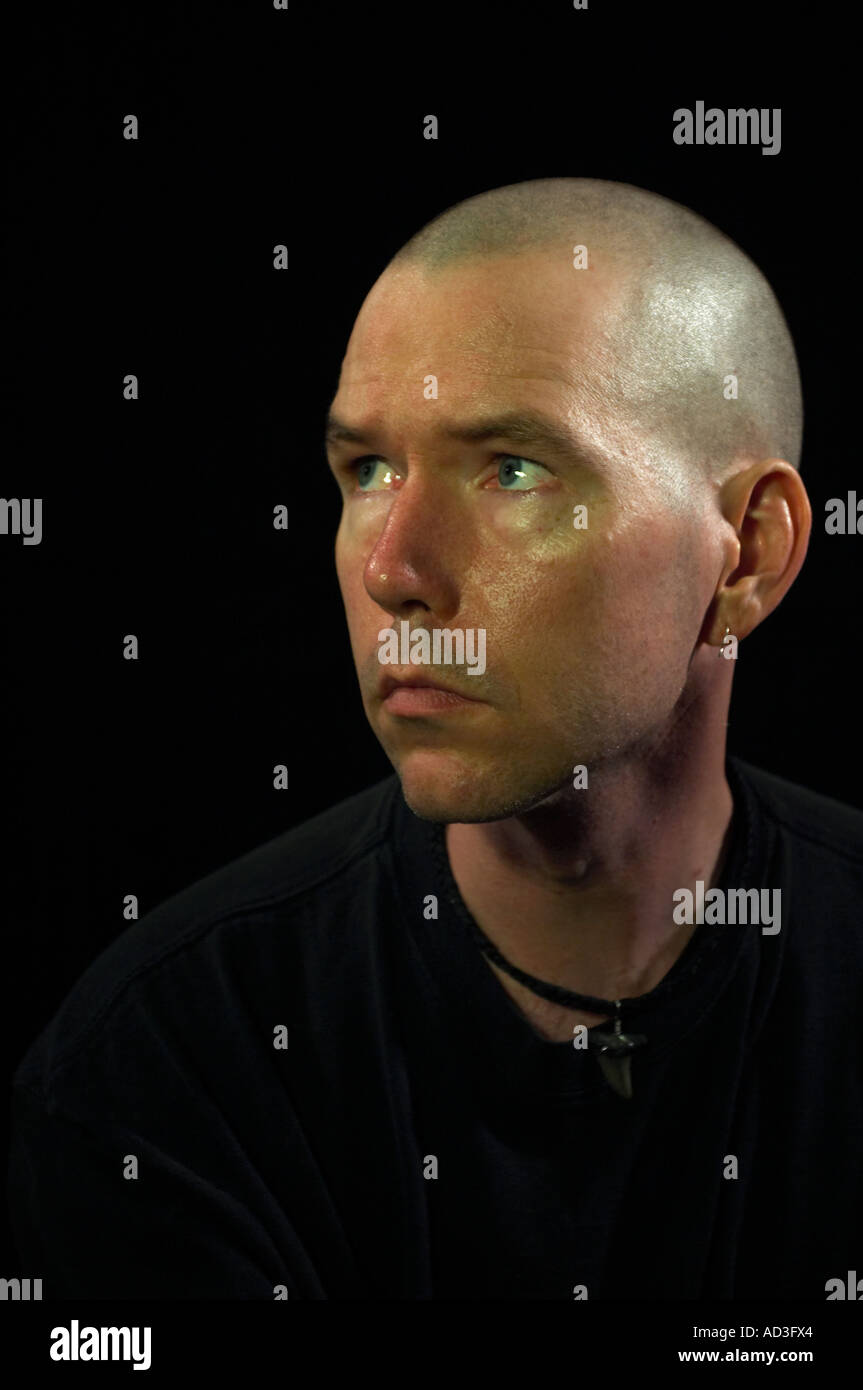 A man with a shaved head in a black shirt on a black background looking ...