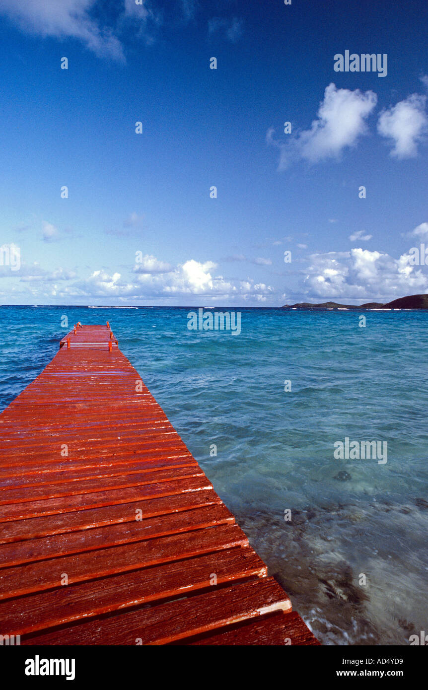 Red wooden sunlit jetty jutting out into an azure blue sea with puffy ...