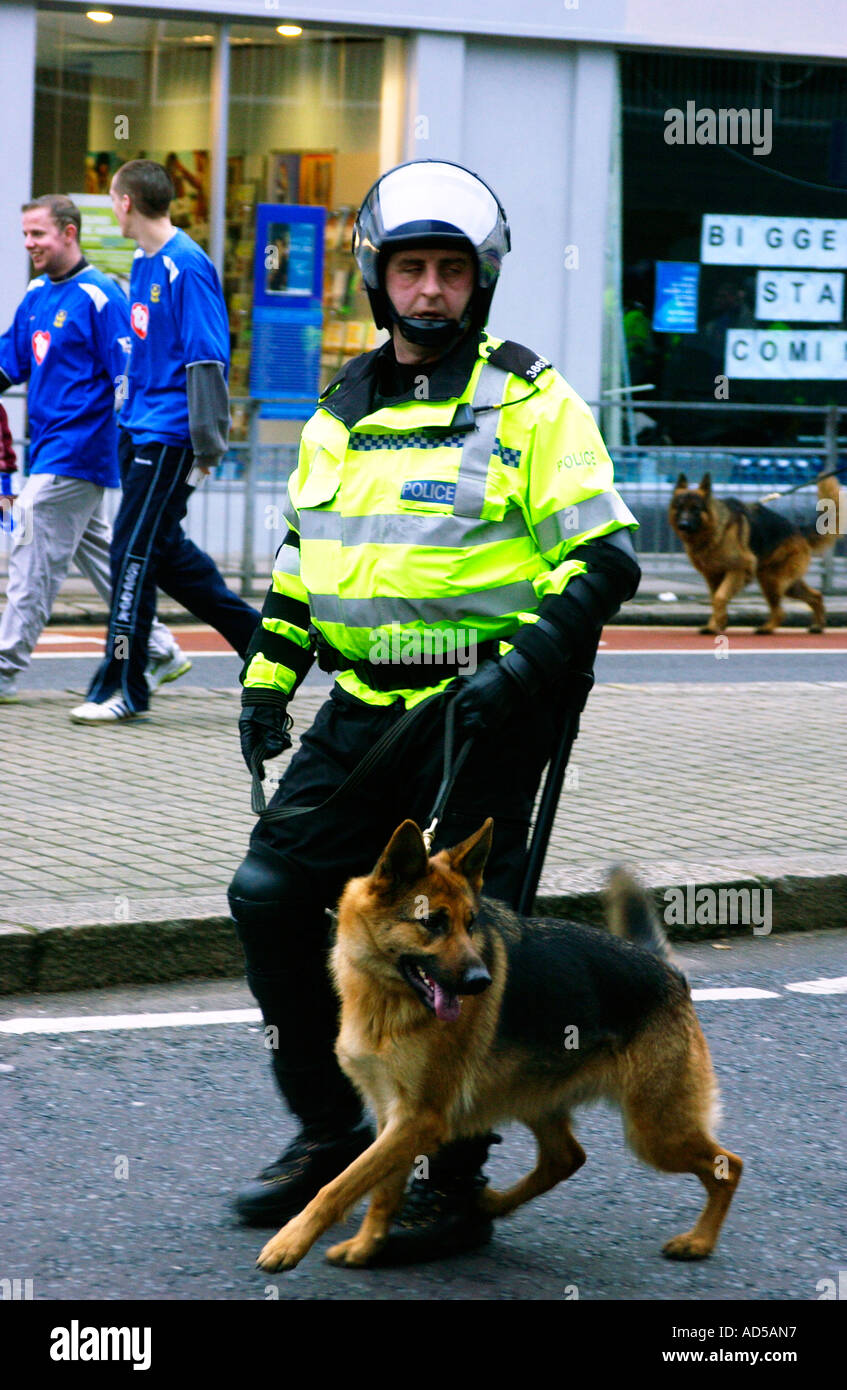 Police handler and dog in riot gear controlling football supporters at ...