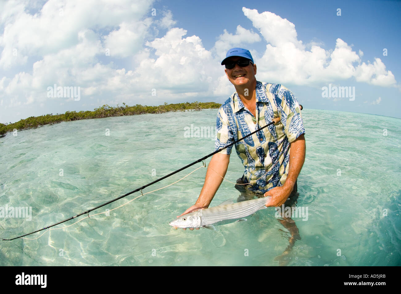 GREATER EXUMA BAHAMAS Fly fisherman releasing Bonefish in emerald green ...