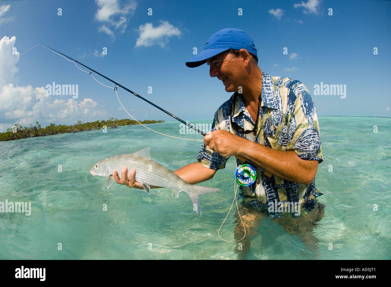 GREATER EXUMA BAHAMA S Fly fisherman releasing Bonefish in emerald ...