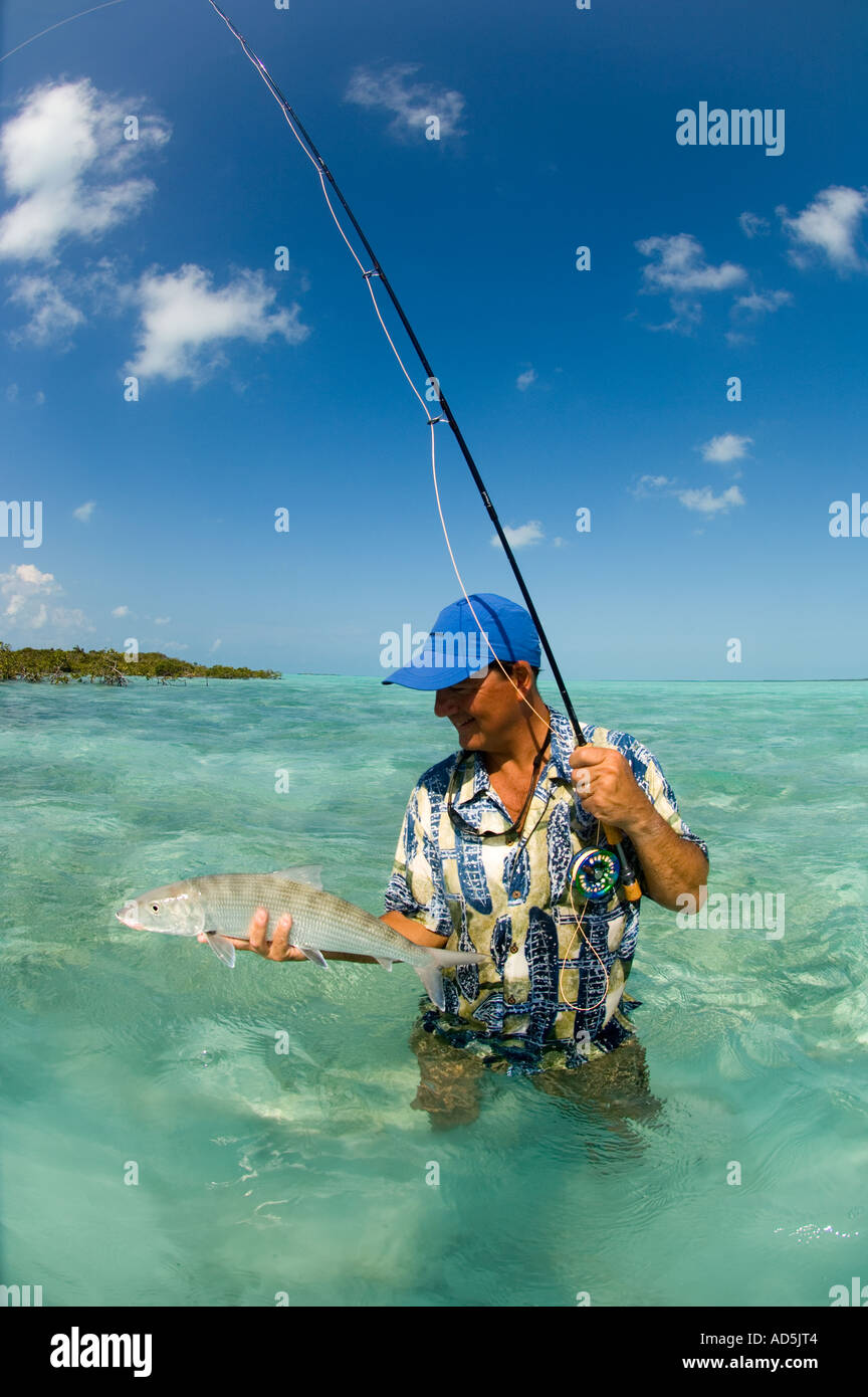 GREATER EXUMA BAHAMAS Fly fisherman releasing Bonefish in emerald green ...