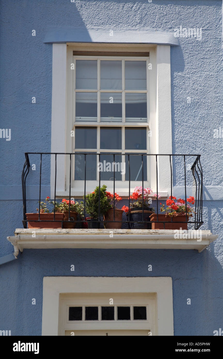 Pastel blue house with white sash windows and red geraniums on balcony ...