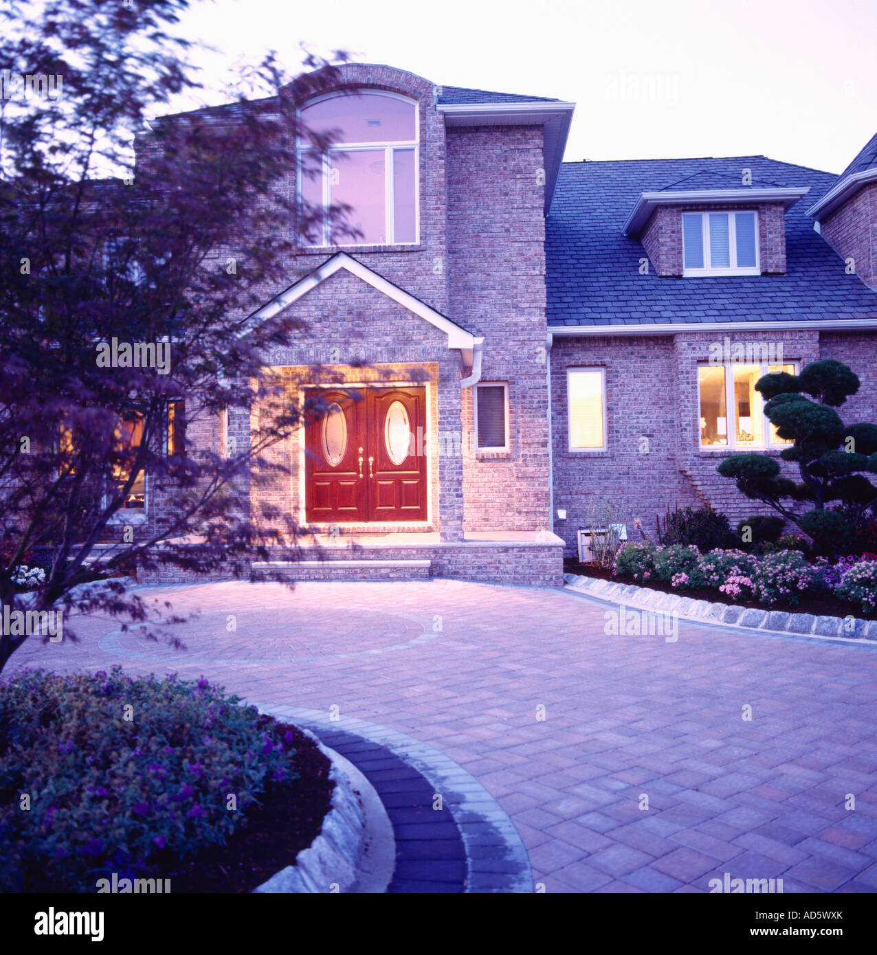Paved drive to newbuild house with lighted windows in early evening ...