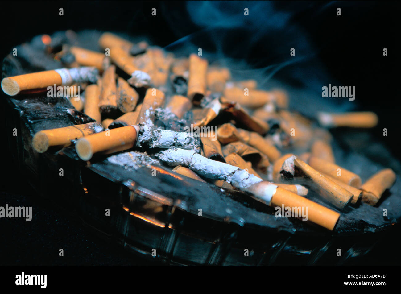 Overfull ashtray with smoking cigarette butts Stock Photo - Alamy