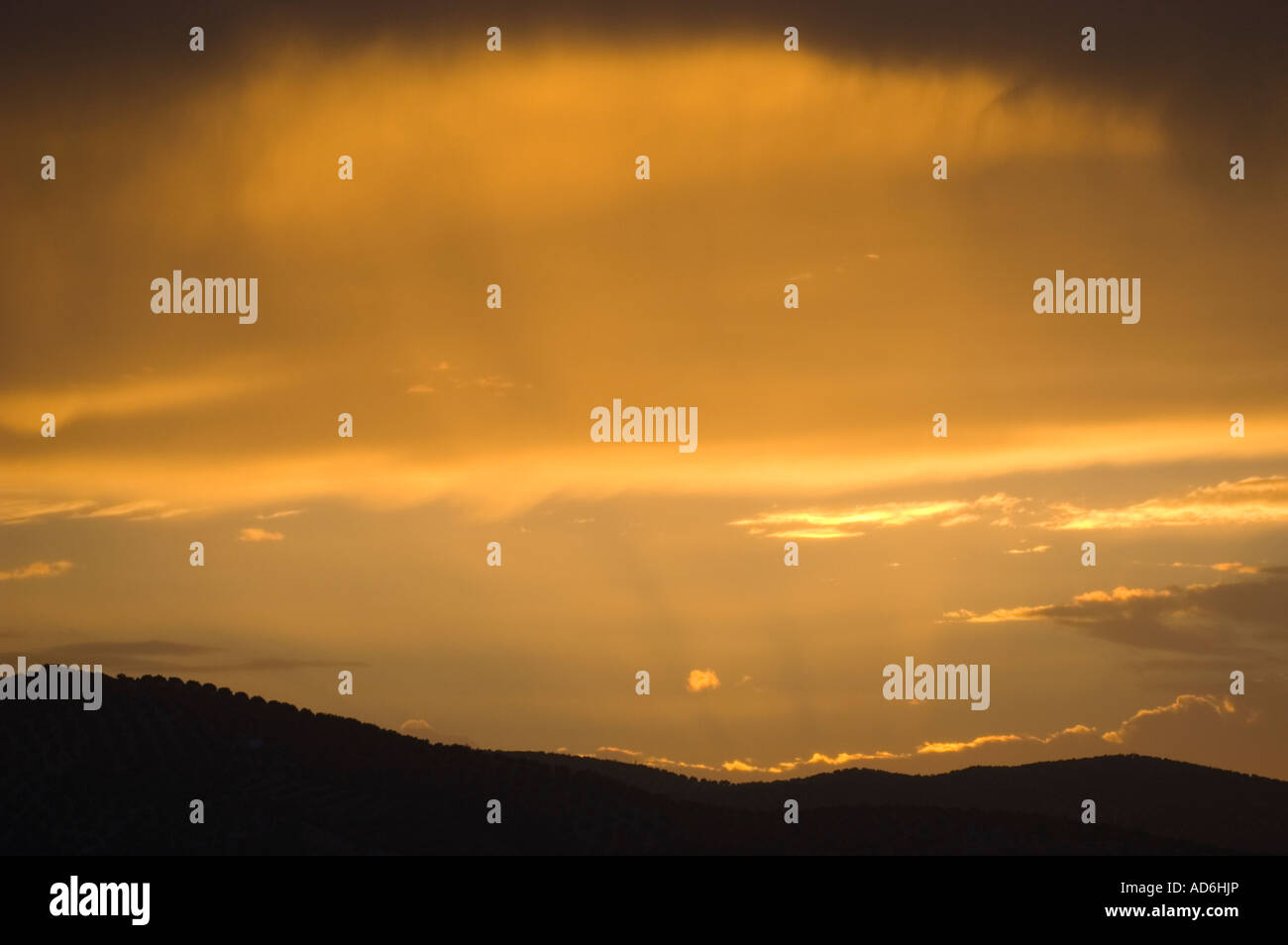 Brooding sky at dusk over a line of distant hills with sun rays ...