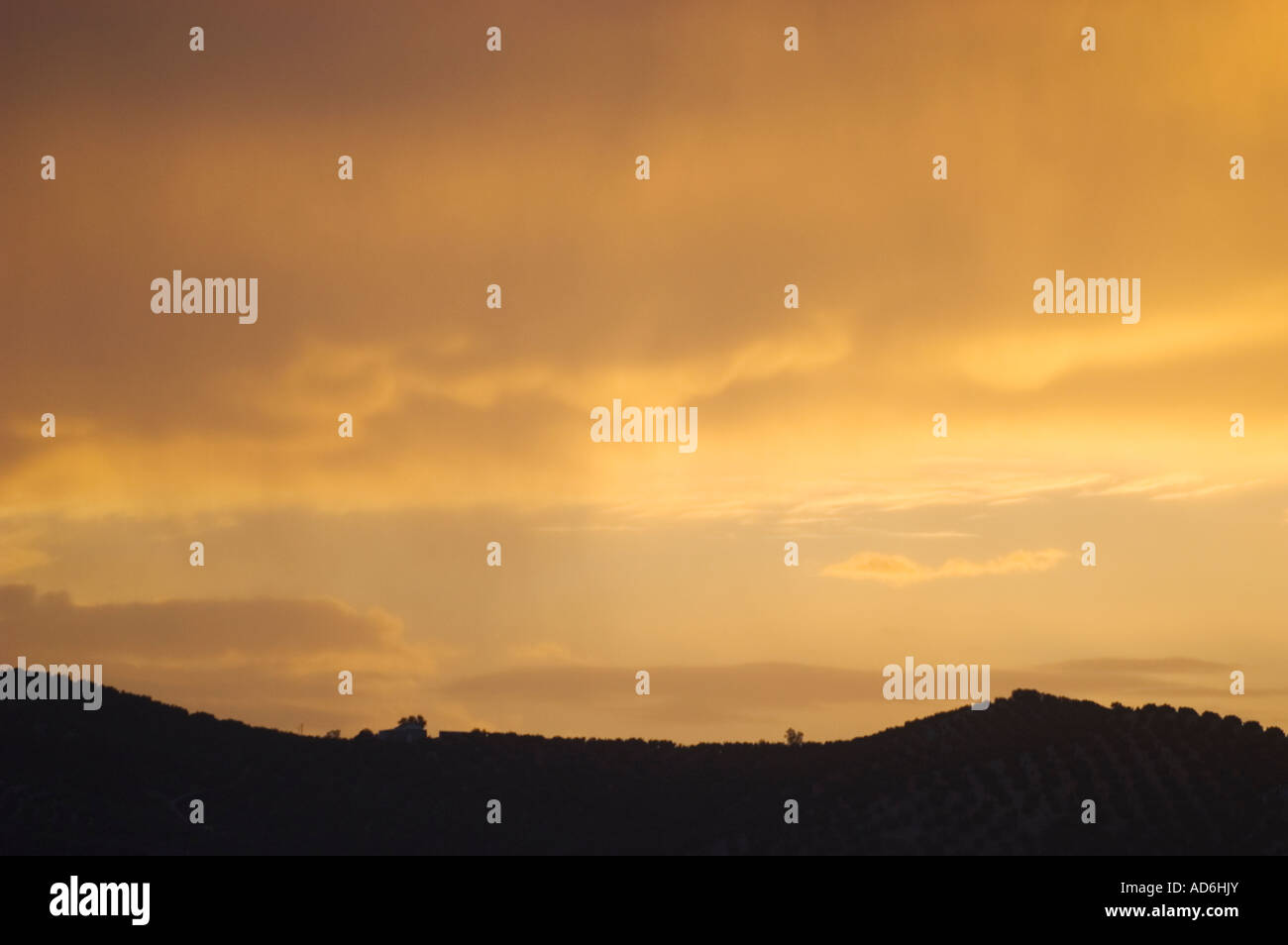 Brooding sky at dusk over a line of distant hills, rich gold and orange ...