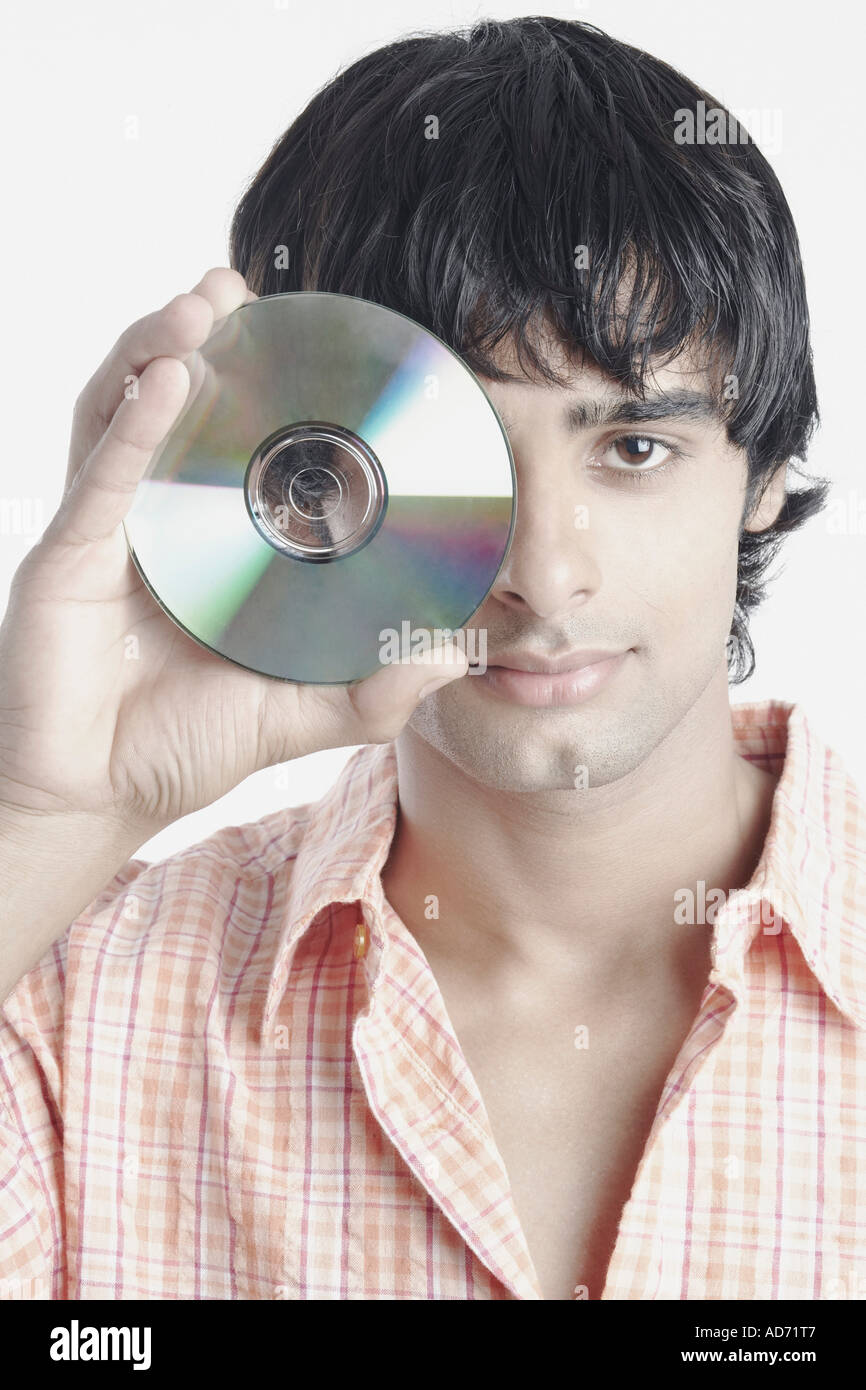 Portrait of a young man holding a compact disk in front of his face ...