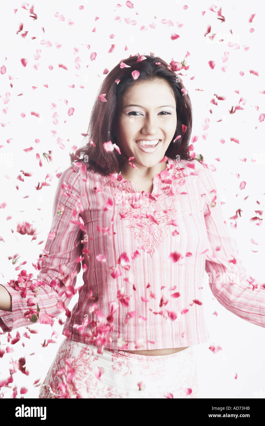 Portrait of a young woman standing with rose petals falling on her ...
