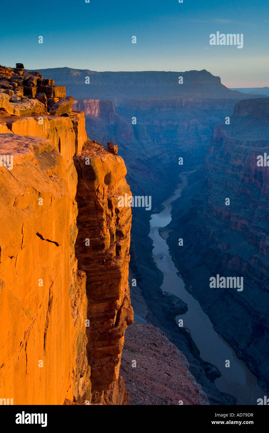 Golden sunrise light on steep sheer rock cliff above the Colorado River ...
