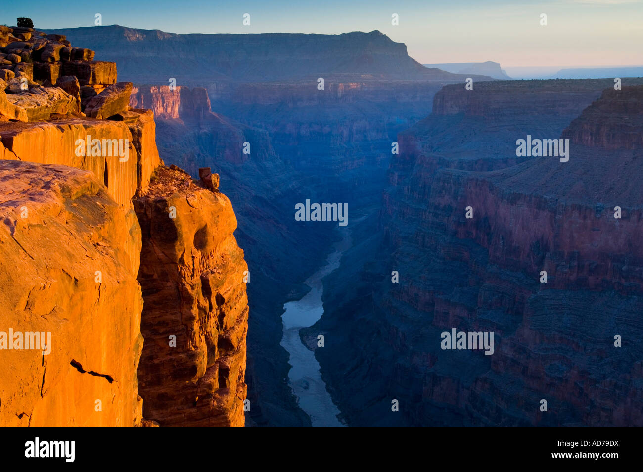 Golden sunrise light on steep sheer rock cliff above the Colorado River ...