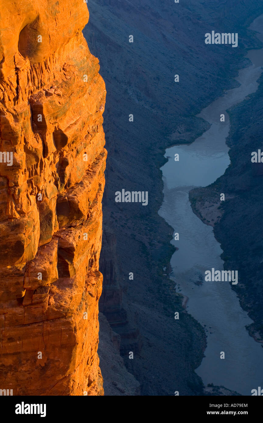 Golden sunrise light on steep sheer rock cliff above the Colorado River ...