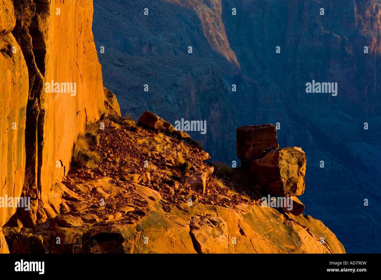 Golden sunrise light on boulder at the edge of a steep sheer rock cliff ...
