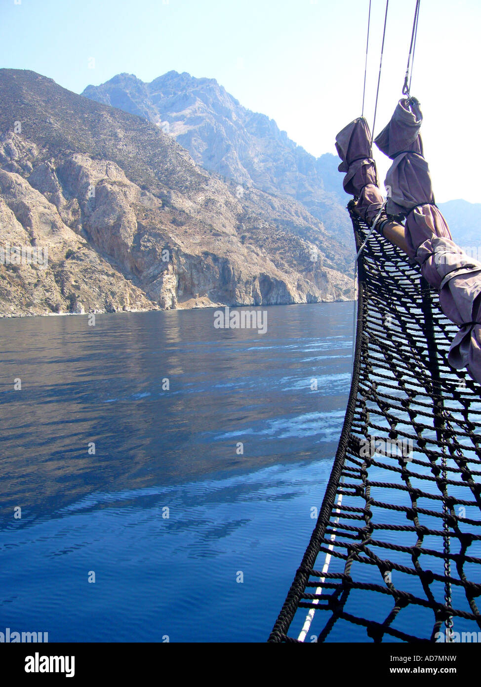 rope netted bow of a wooden sail boat approaching rocky shore line ...