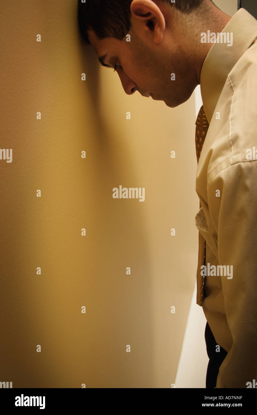 Frustrated man leaning head against wall Stock Photo - Alamy