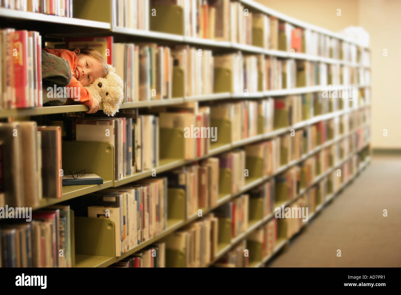 Little girl diding in library shelf Stock Photo - Alamy