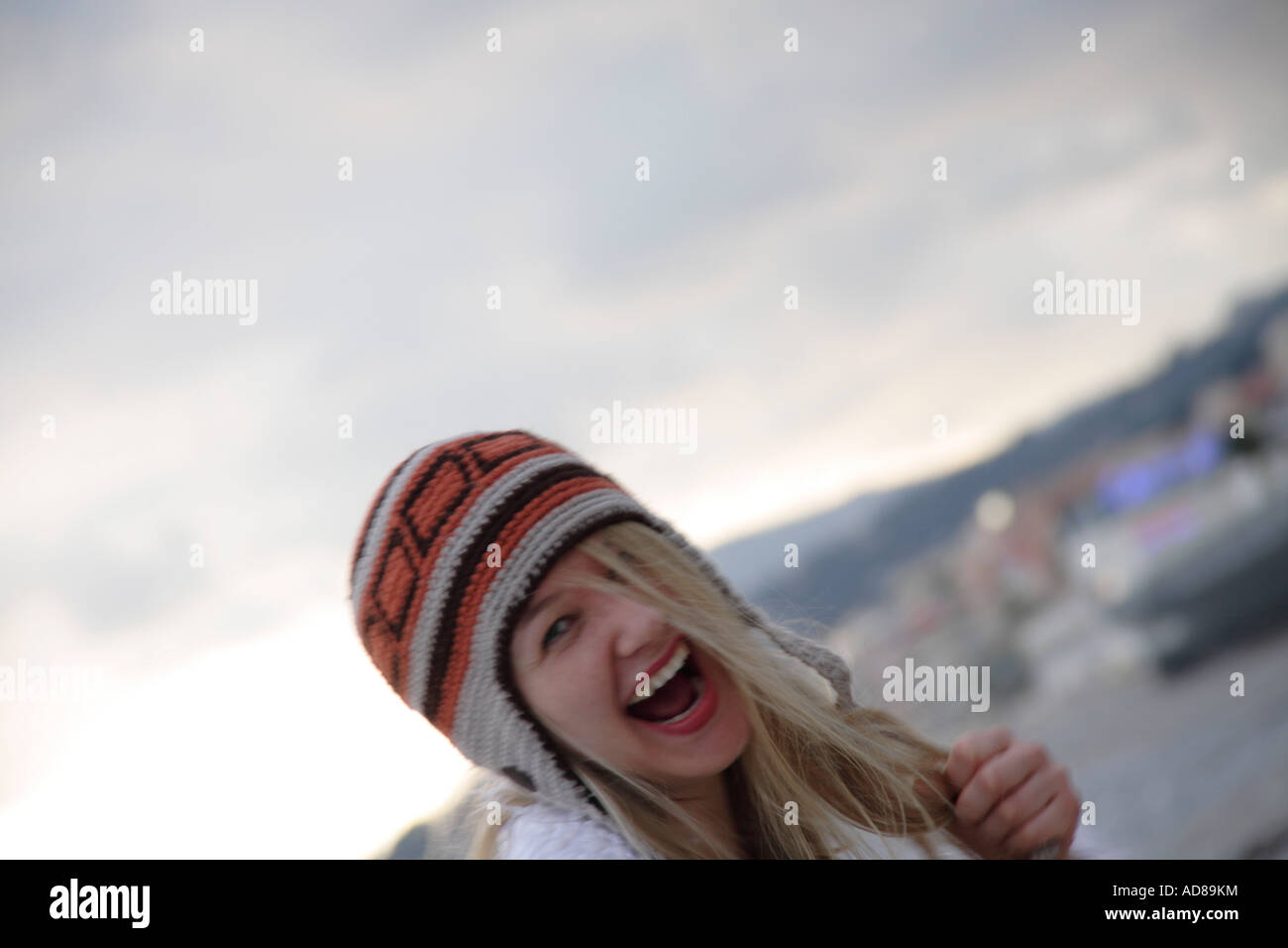 Young woman wearing knitted cap, running and laughing at the beach ...