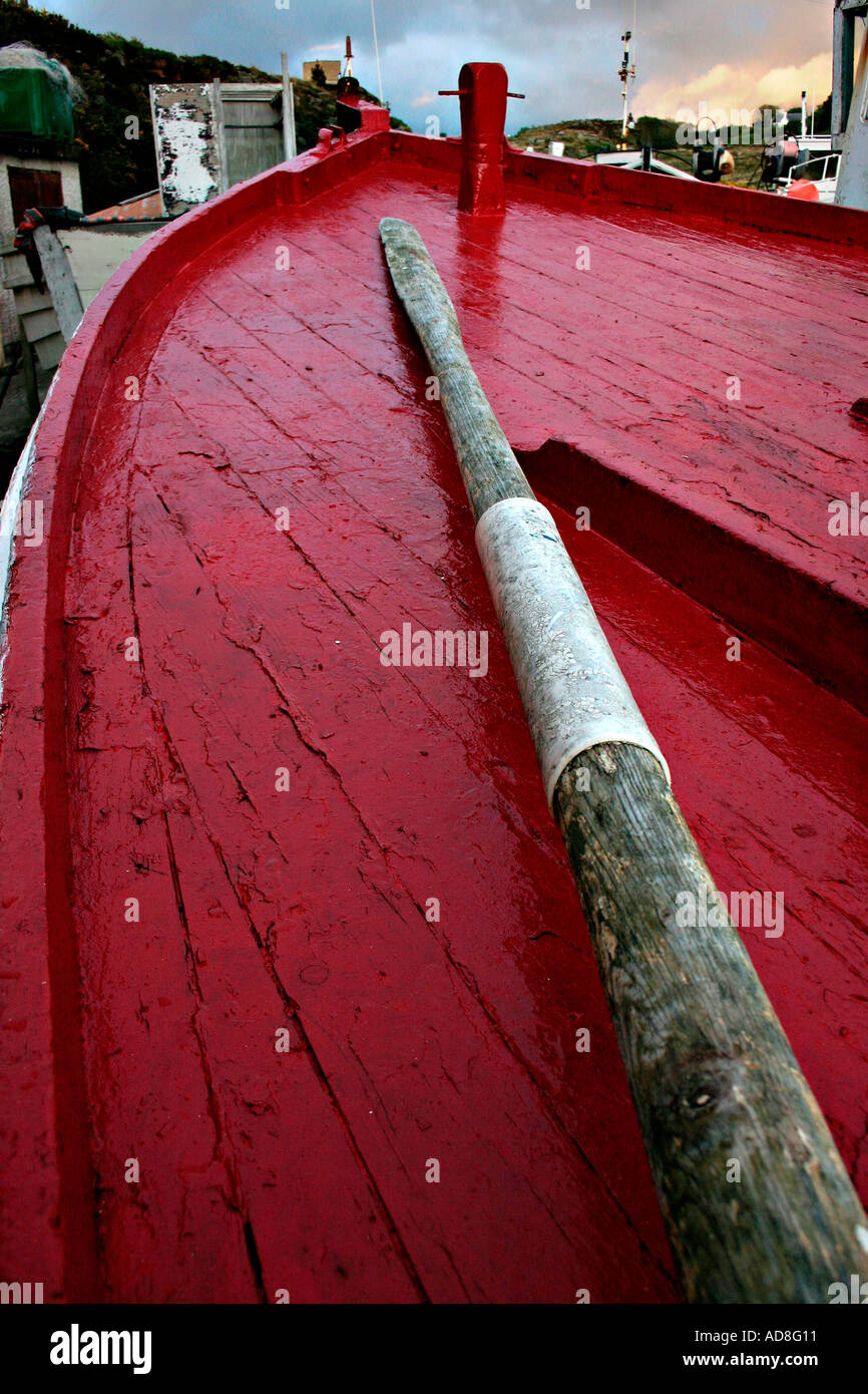 An oar rests atop a freshly painted red deck of a wood planked boat ...