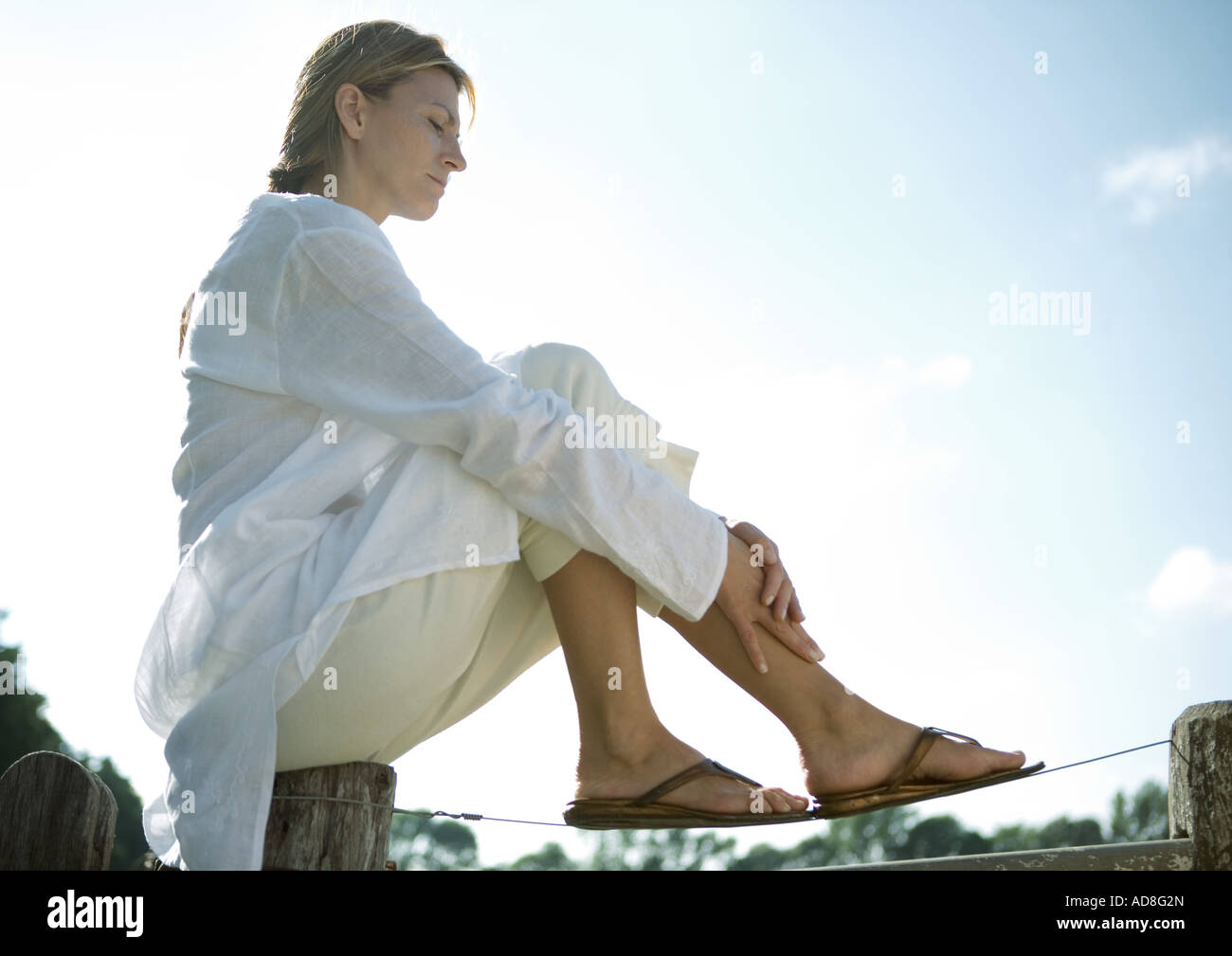 Woman sitting on top of fence, low angle view Stock Photo - Alamy
