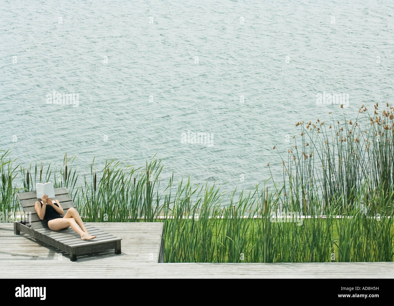 Woman reclining on lounge chair, reading, next to lake Stock Photo - Alamy