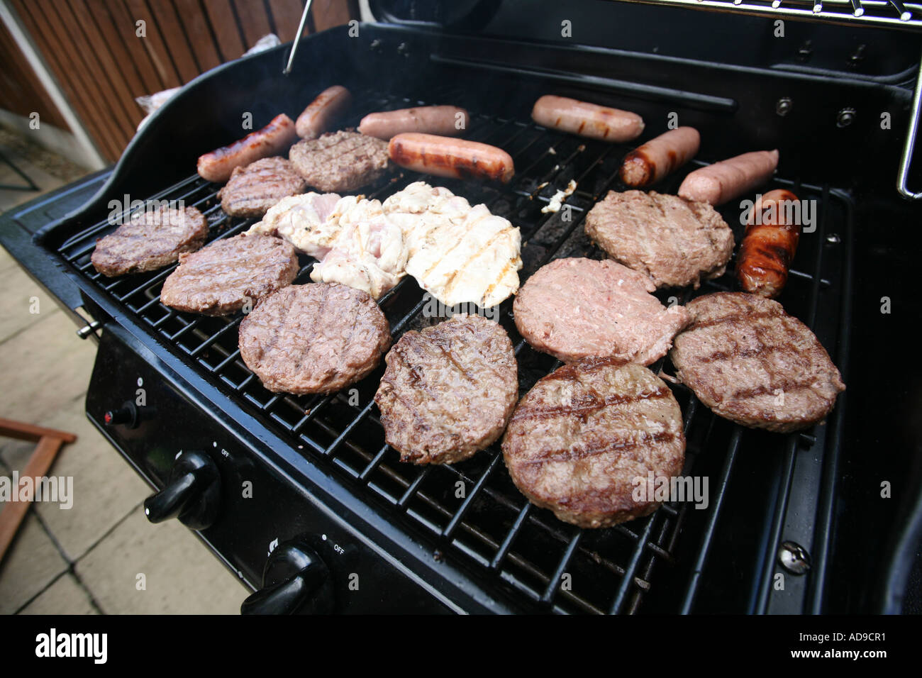 Various meats being cooked on a gas powered barbecue Stock Photo - Alamy