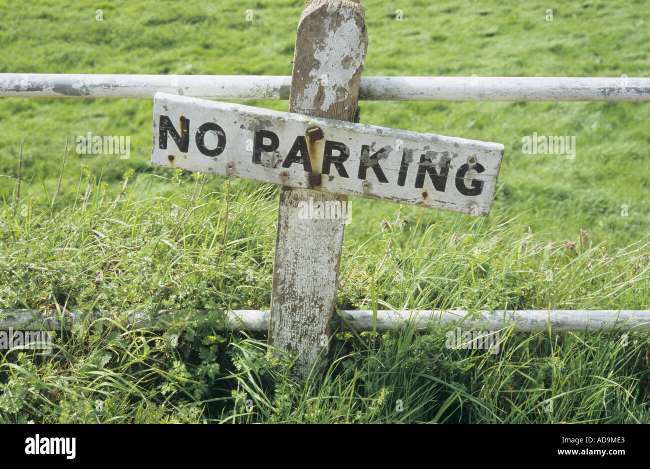 A weathered painted sign attached to a post with railings stating No ...