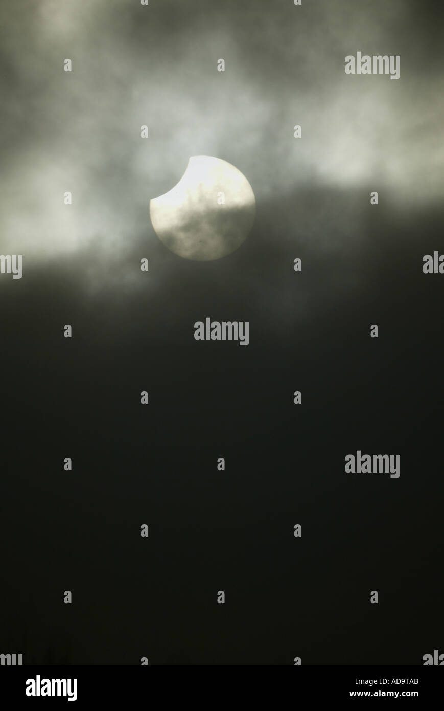 Seen through translucent drifting clouds an eclipse of the sun takes ...