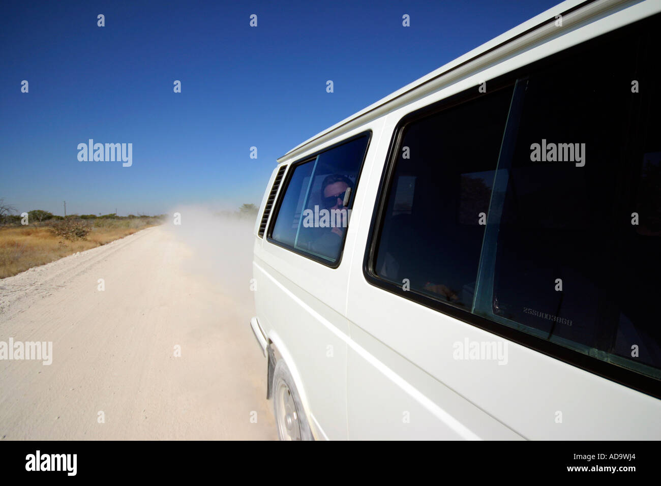 woman looking from window of White minibus travelling down gravel road ...