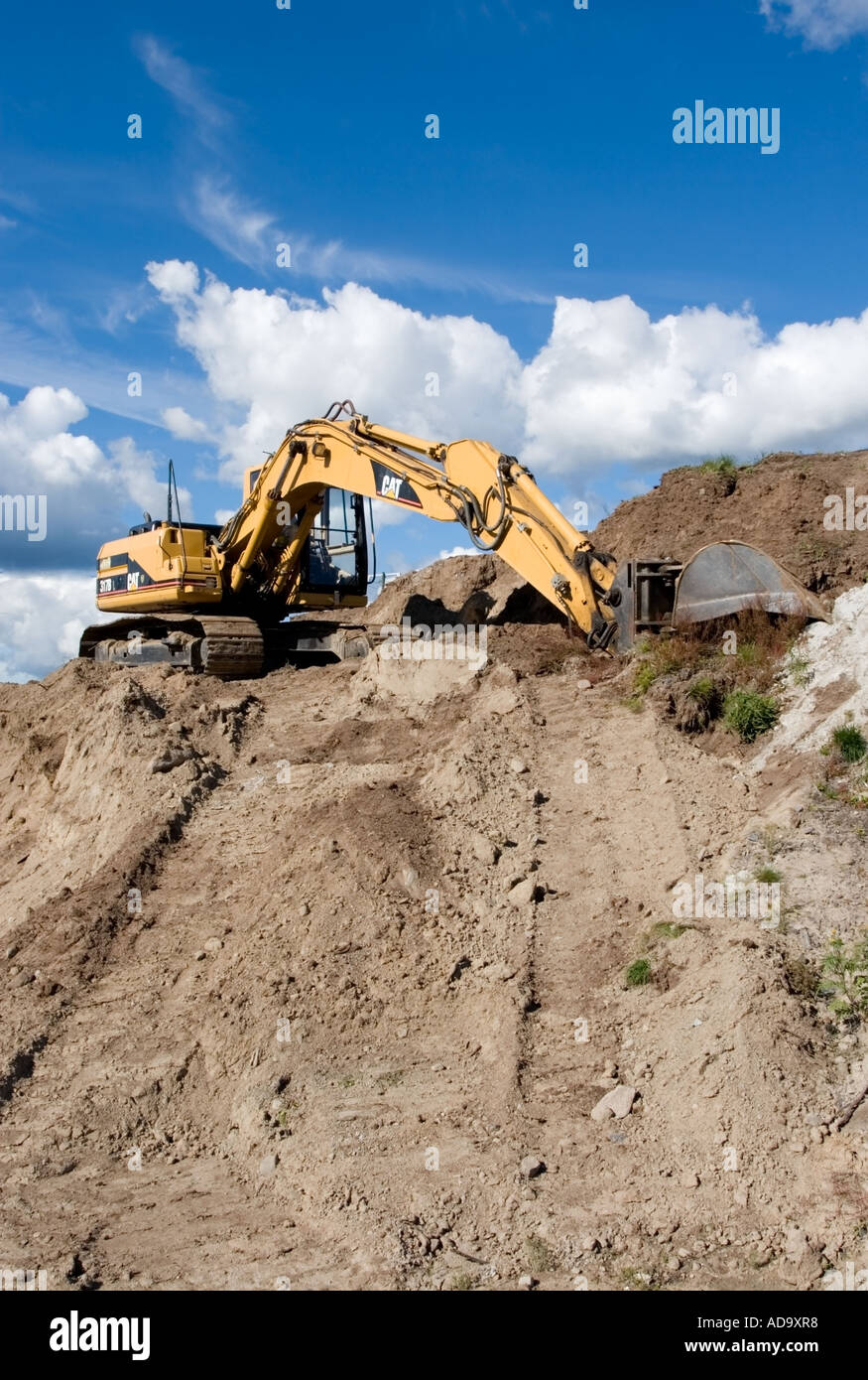 Yellow Caterpillar (CAT) digger on top of a sand mound against blue sky ...