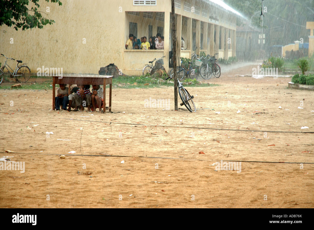 Children hiding under a desk outside during heavy rain in a school ...