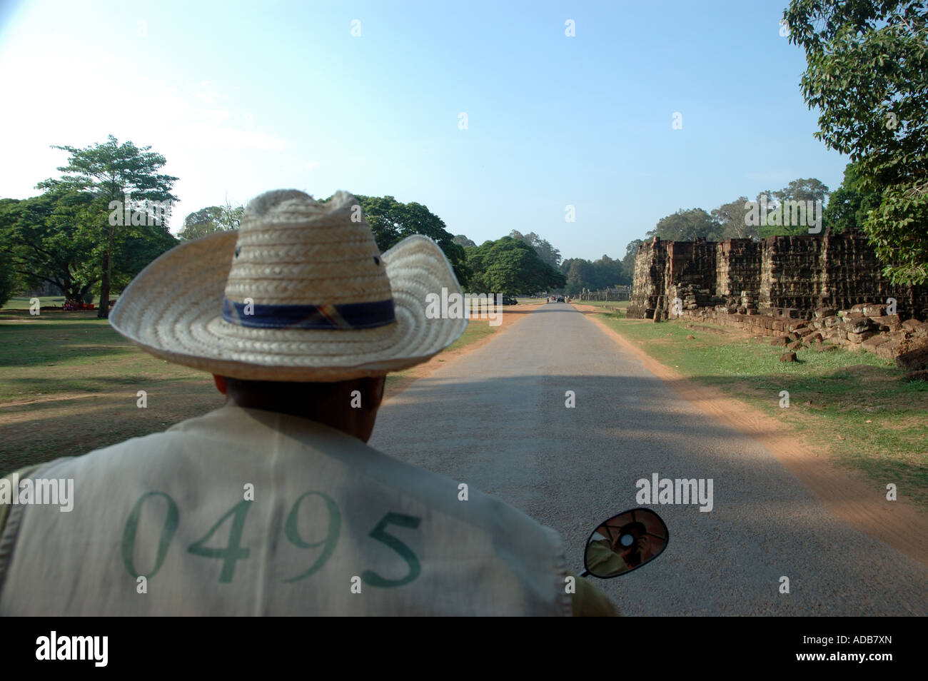 A tuk tuk driver with a hat driving through Angkor Wat complex ...