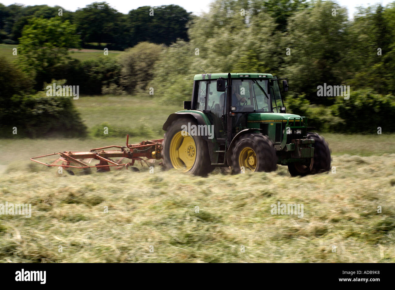 Tractor turning grass for hay 2 Stock Photo - Alamy
