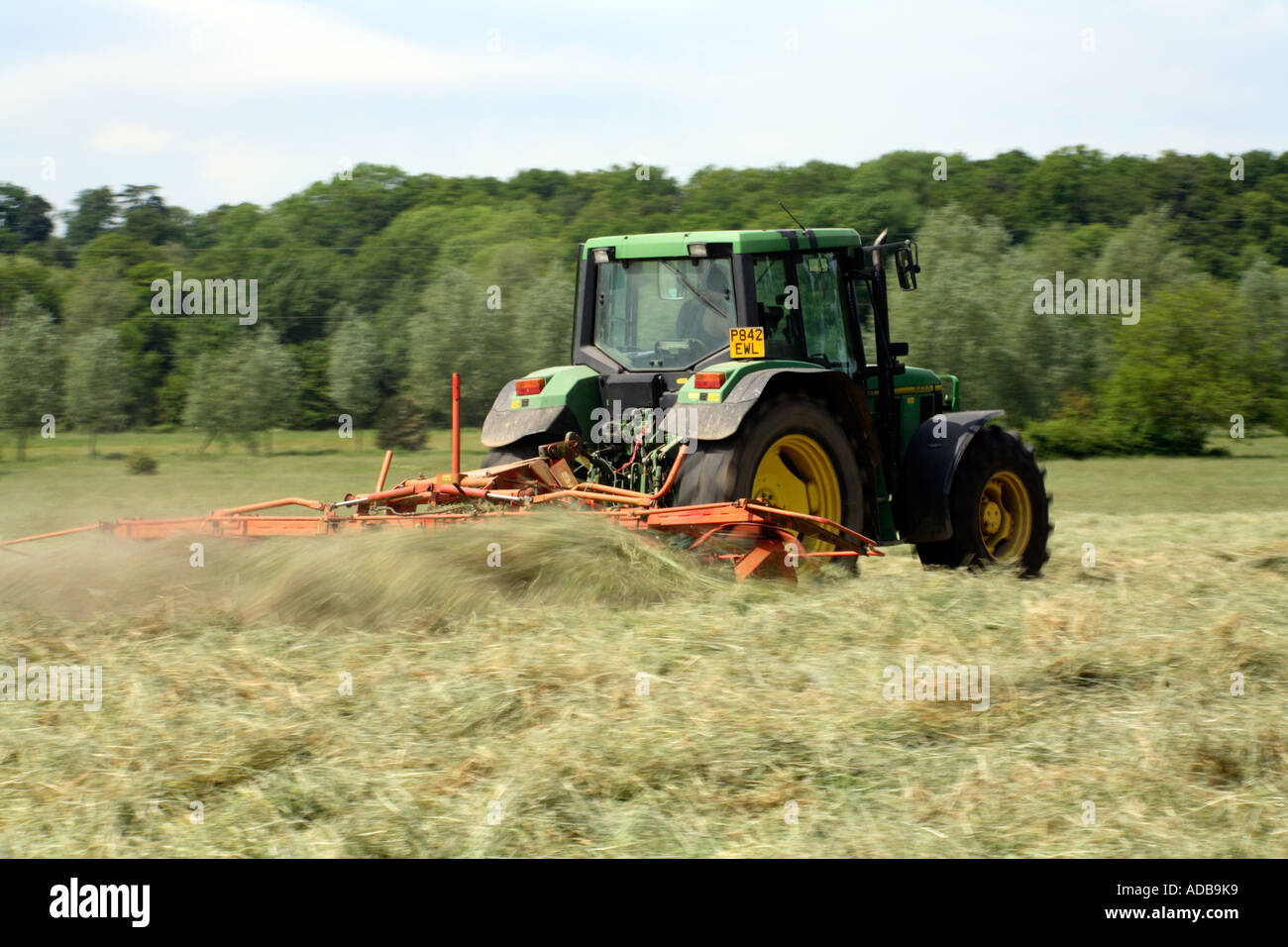 Tractor turning grass for hay 1 Stock Photo - Alamy