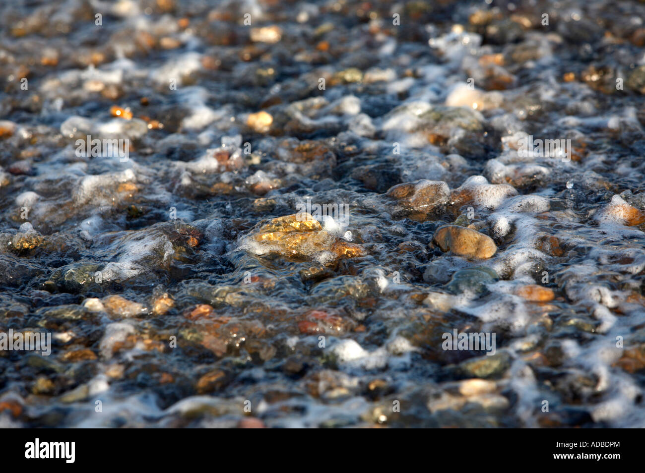 sea water and foam rushing over pebbles on a stony beach in county ...