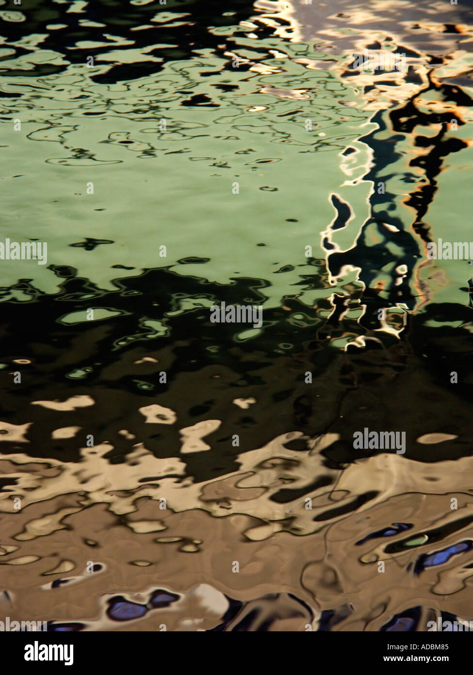 Abstract green black and tan reflection in a swiftly flowing river ...