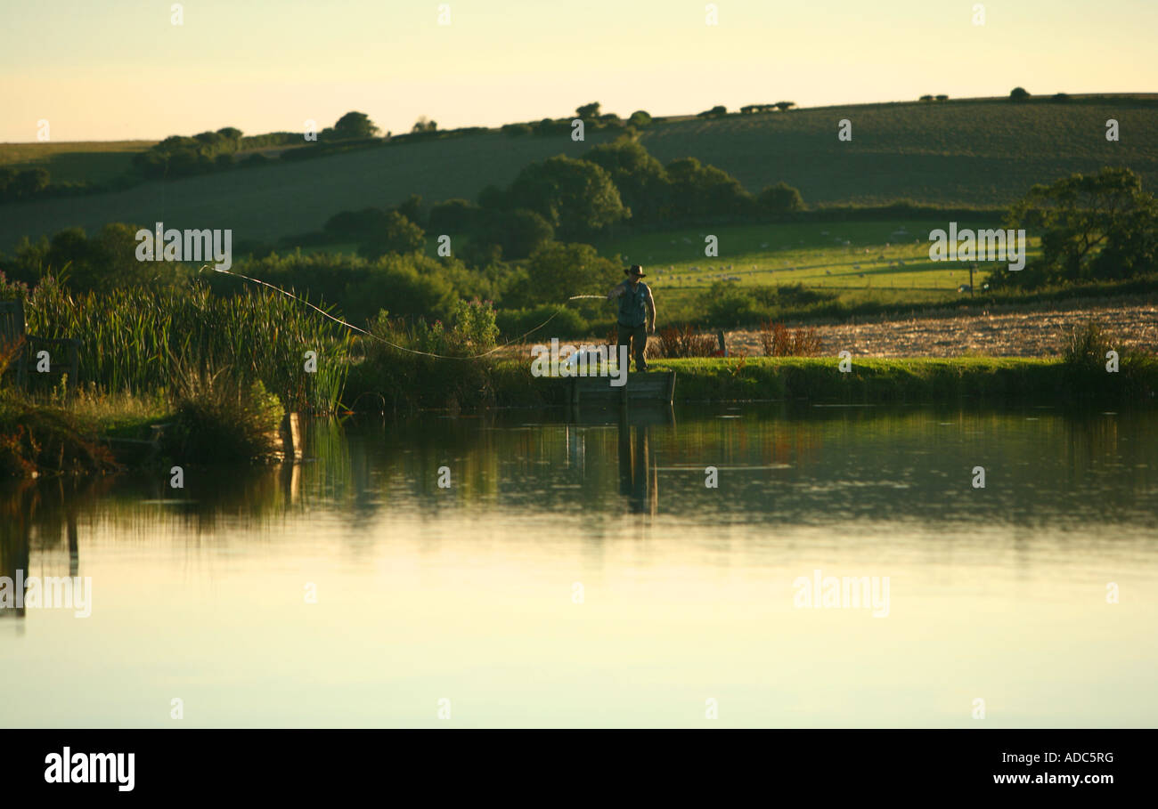 Man fly fishing in the evening sun with rural countryside in the ...