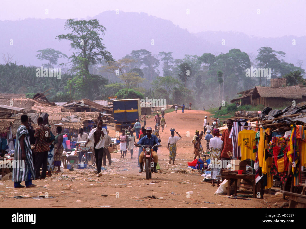 Merchant stalls line a dusty dirt road through a village in the west of ...