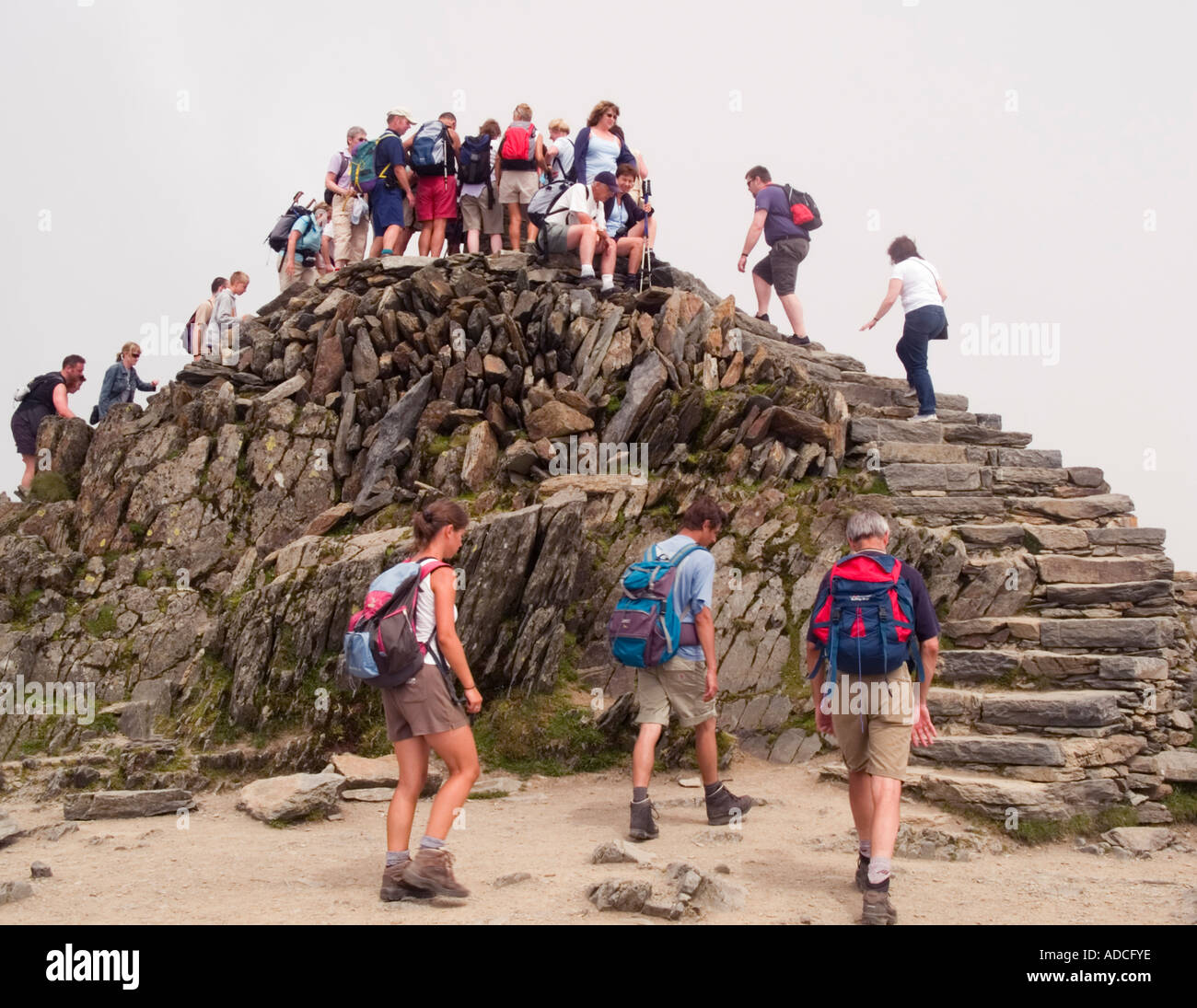 Walkers climbing on Mount Snowdon summit cairn on busy weekend in ...