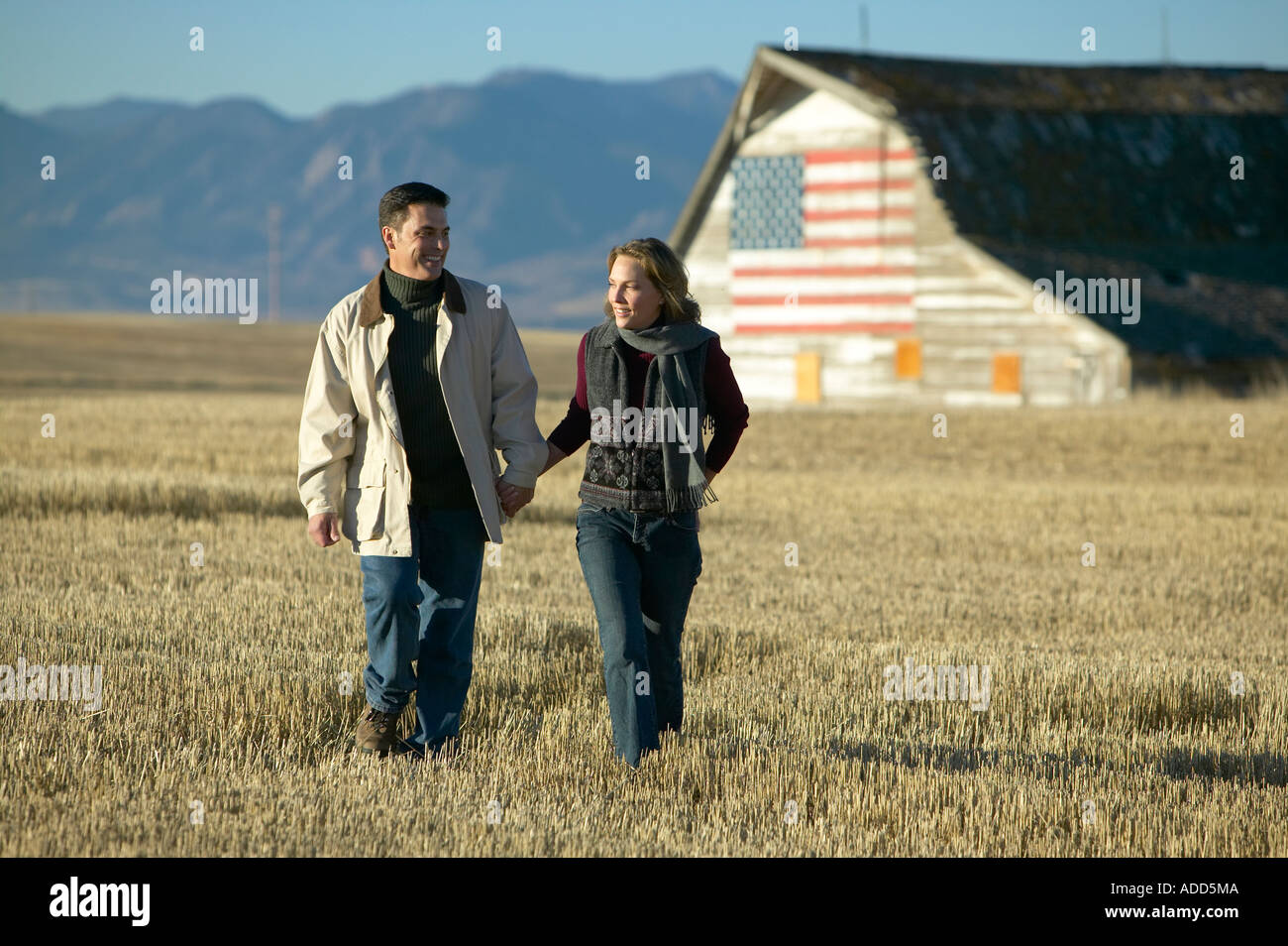Man and women walking through cut grass fields in Fall with barn and ...