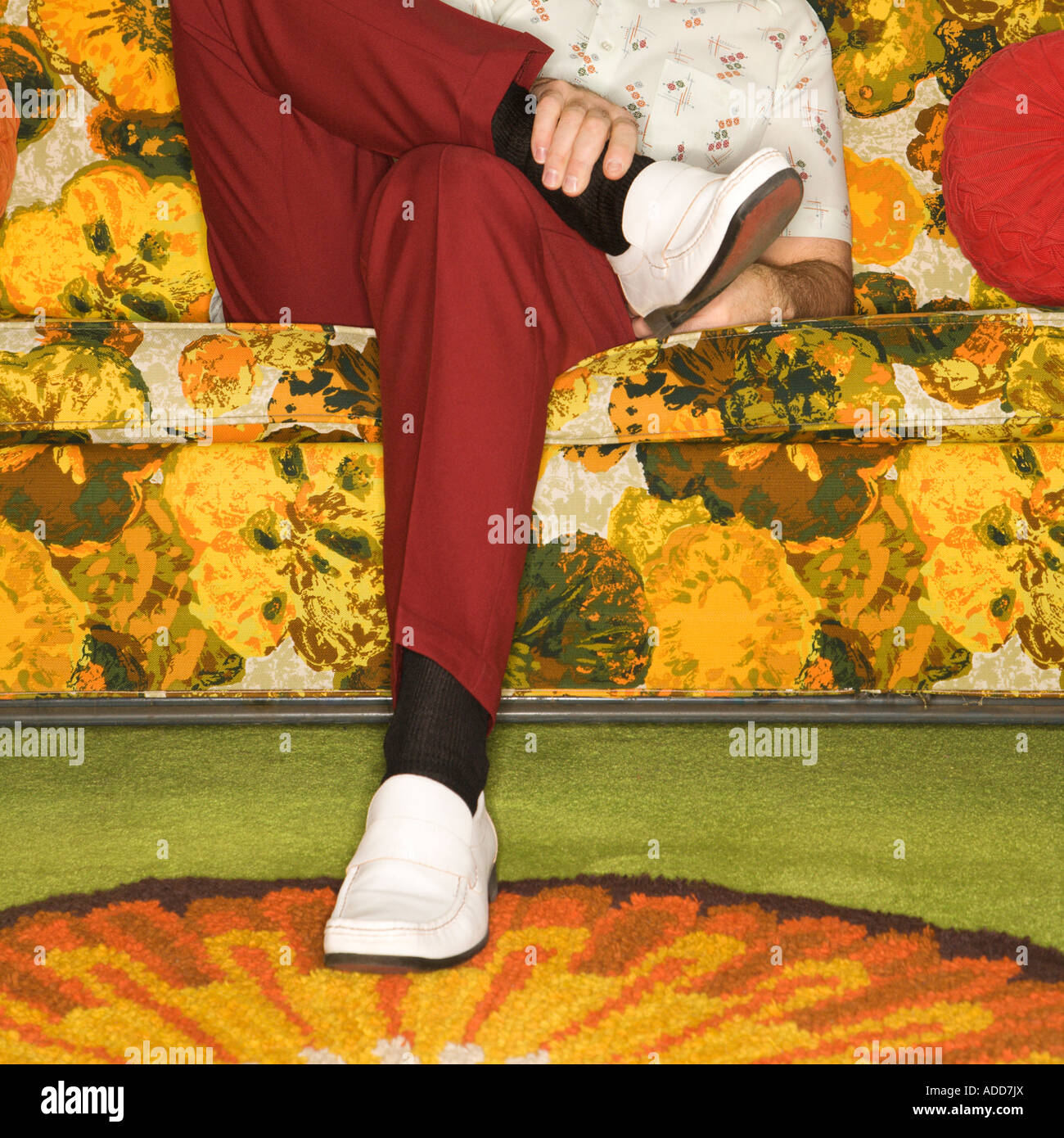 Caucasian mid adult man sitting on colorful retro sofa looking bored ...