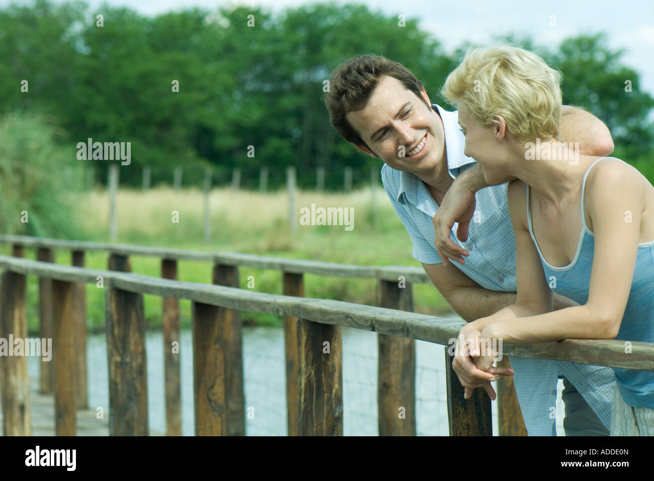 Couple standing on footbridge, leaning against rail, talking Stock ...