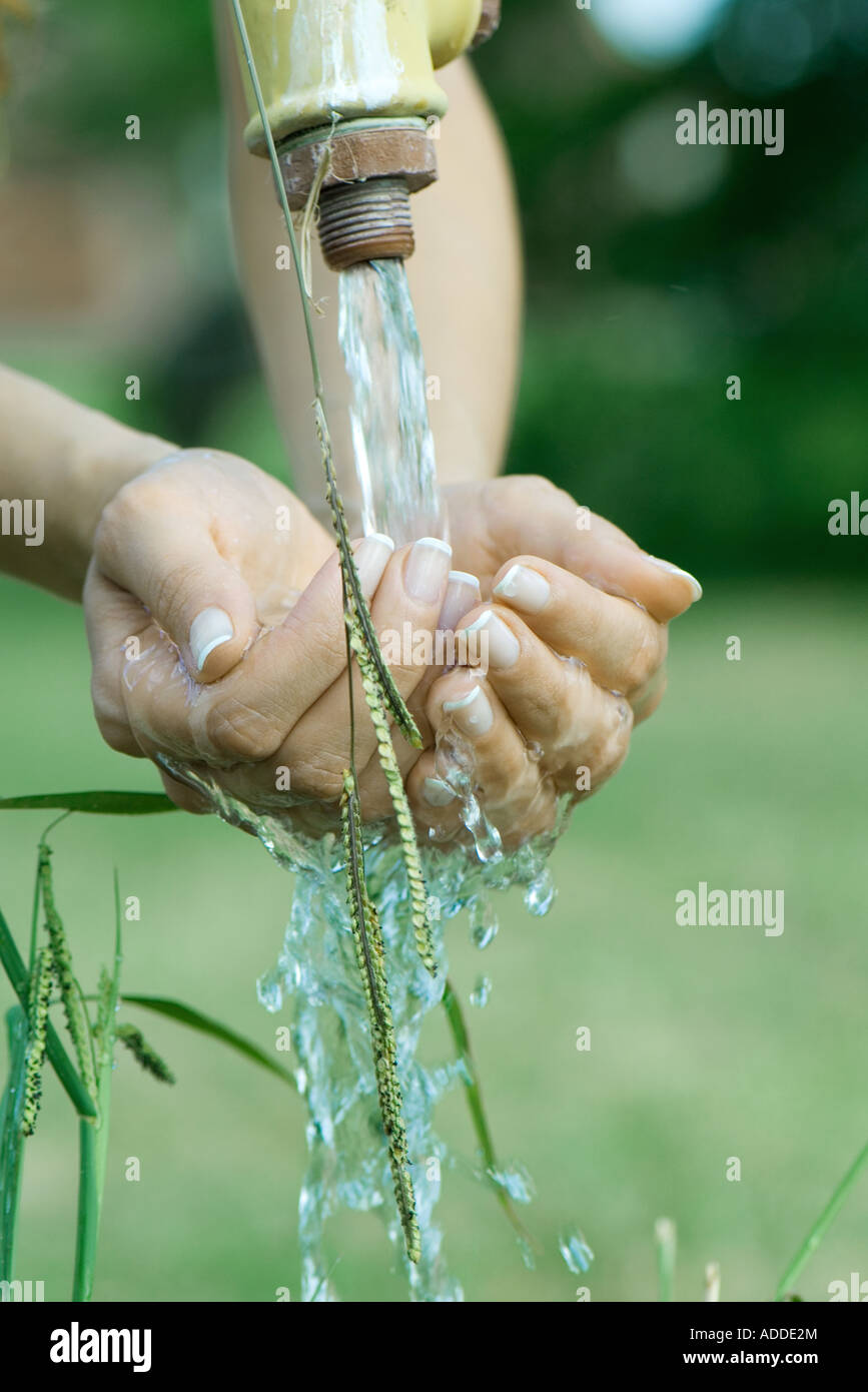 Woman cupping hands under outdoor faucet, close-up, cropped view of ...
