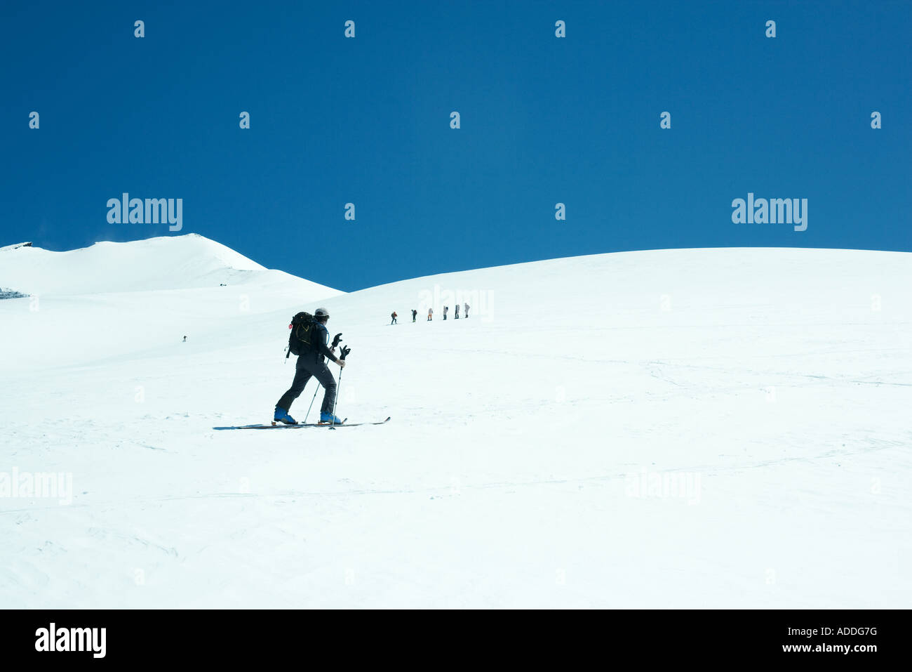 Skier going across snowy landscape, looking toward group of skiers in ...