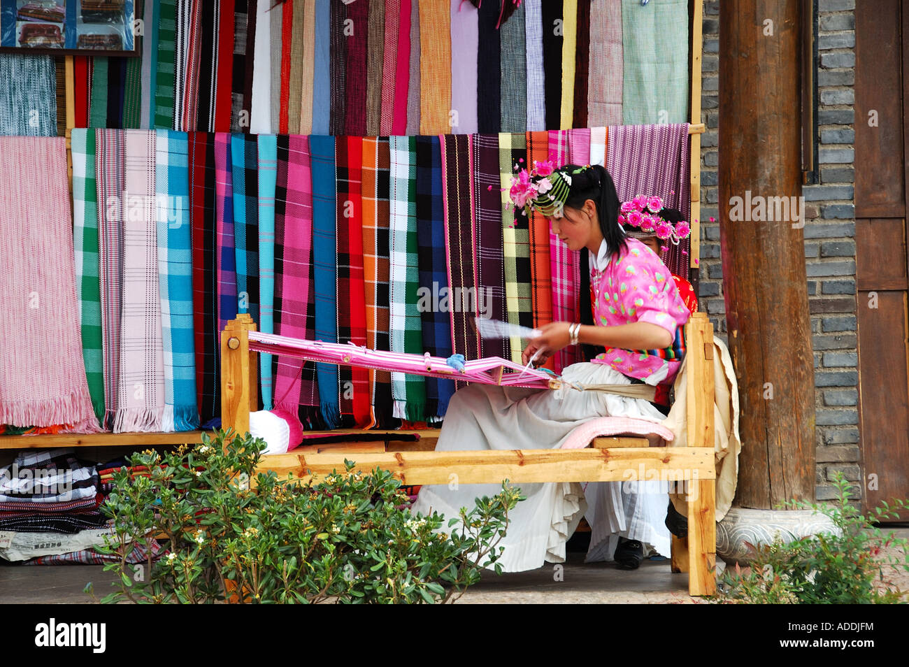 A young women in traditional Naxi dress hand weaving scarves in old ...