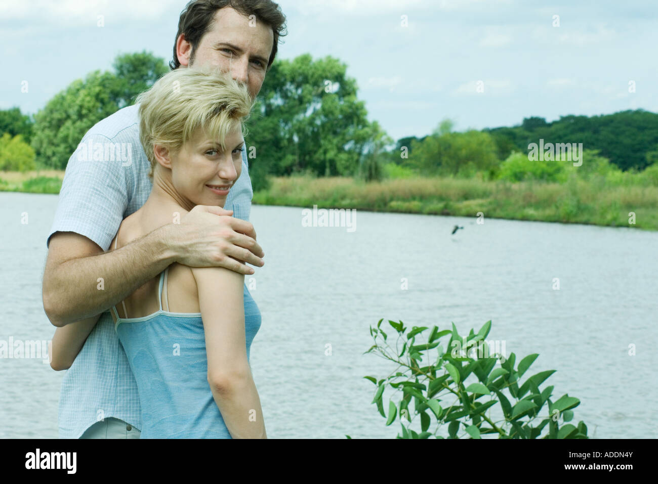 Couple standing by lake, looking over shoulders at camera Stock Photo ...