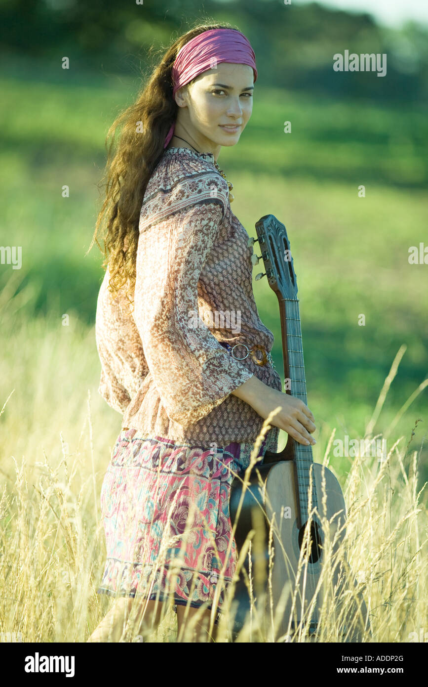Young hippie woman walking through field, holding guitar Stock Photo ...